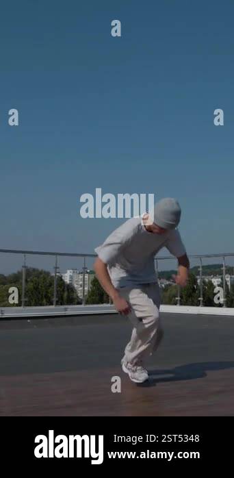 Vertical. The guy coolly dances breakdance on the roof of the house. A man dances an energetic ...