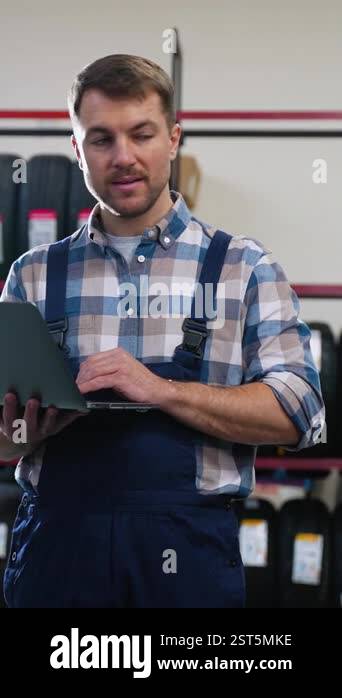 A store employee in uniform checks tire inventory using a laptop. He ...