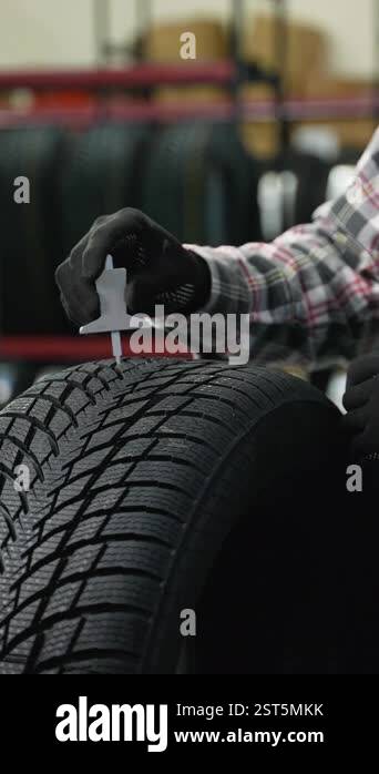 An African American mechanic in overalls and gloves uses a tread depth ...