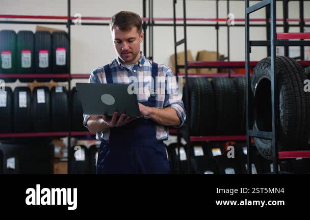 A store employee in uniform checks tire inventory using a laptop. He ...