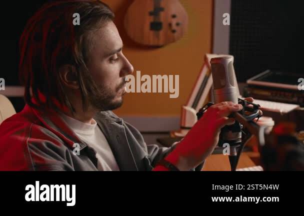 Medium closeup of Caucasian male musician with dreadlocks setting up ...
