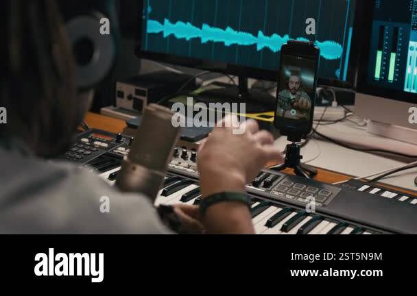 Medium over-shoulder shot of young male musician sitting in studio with ...