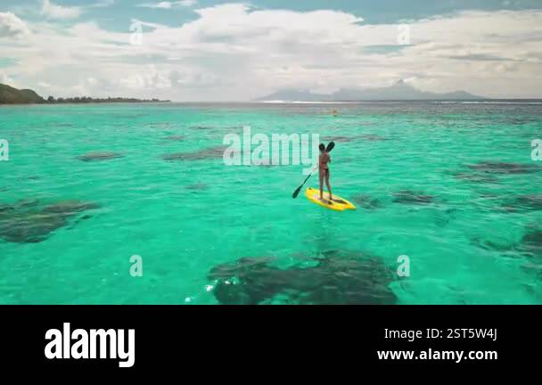 Back view female stand on yellow sup board with paddle. Crystal green ...