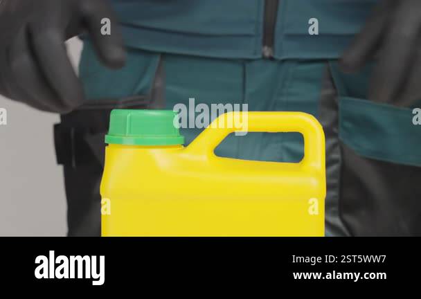 A figure in black gloves pours bleach into a yellow container, hinting ...