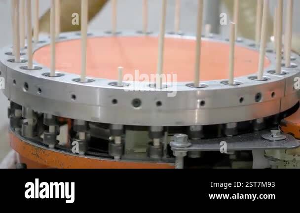 A machine processes wooden dowels, arranging them vertically in a ...