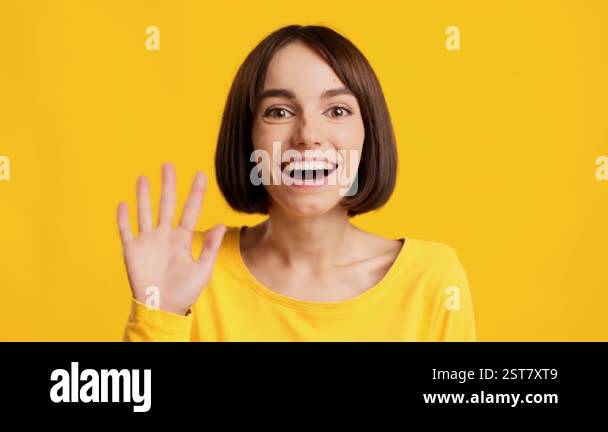 Young lady joyfully waving and smiling, exuding positivity and warmth ...