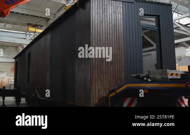 A modern prefabricated modular home with dark wood paneling is securely ...