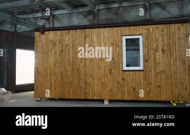 A compact wooden modular house stands inside a factory during its ...