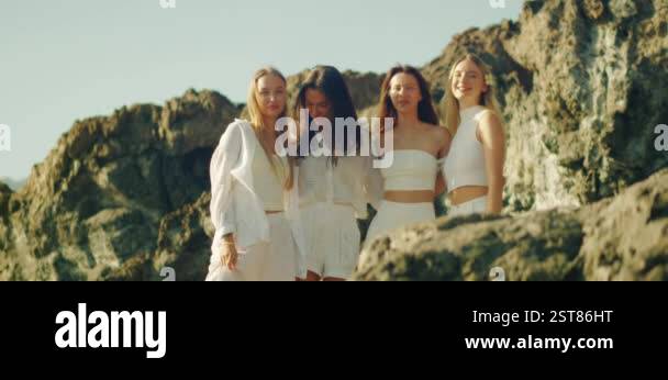 Four young women smiling while standing close together on a rocky beach ...