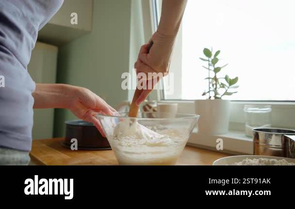 Woman stirring batter in glass bowl with wooden spatula to achieve ...