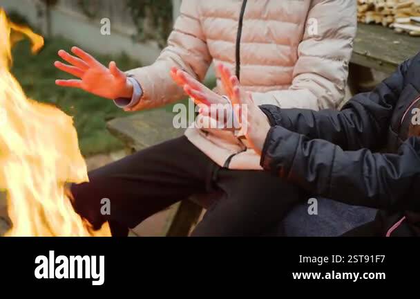 Brother and sister stretching hands towards fire, absorbing heat from ...