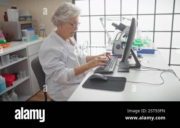 Senior woman scientist typing on computer keyboard in modern laboratory ...