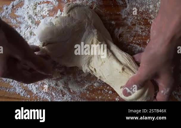 Hands actively kneading and stretching raw dough on a wooden surface ...