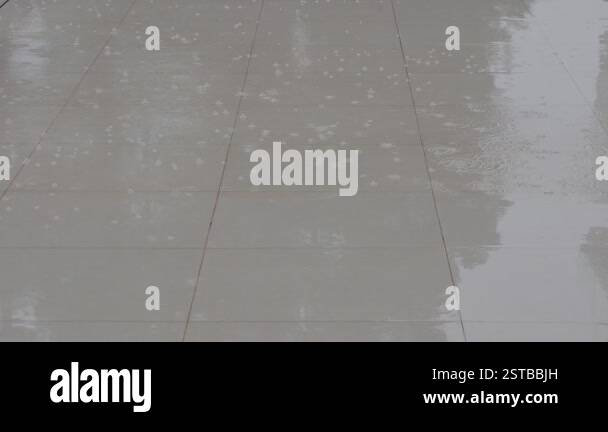 Close-up of a wet tiled floor with rain droplets creating small ripples ...