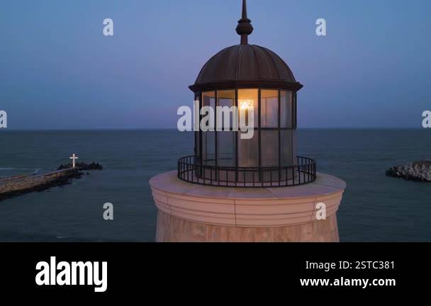 Illuminated lighthouse tower at twilight overlooking the ocean, with a ...