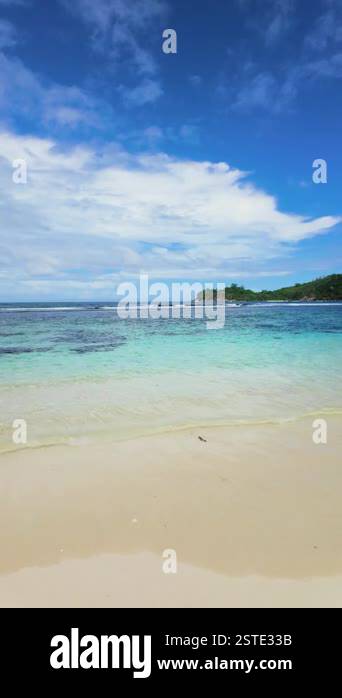 Clear turquoise water meets the white sandy beach under a partly cloudy ...