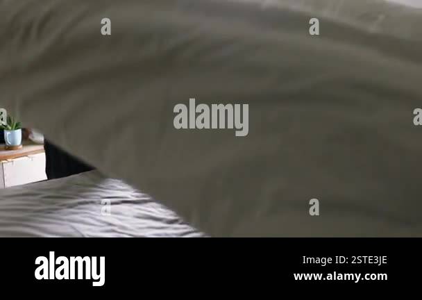 Woman makes the bed, fluffing soft pillows on bed in the bedroom. Young ...