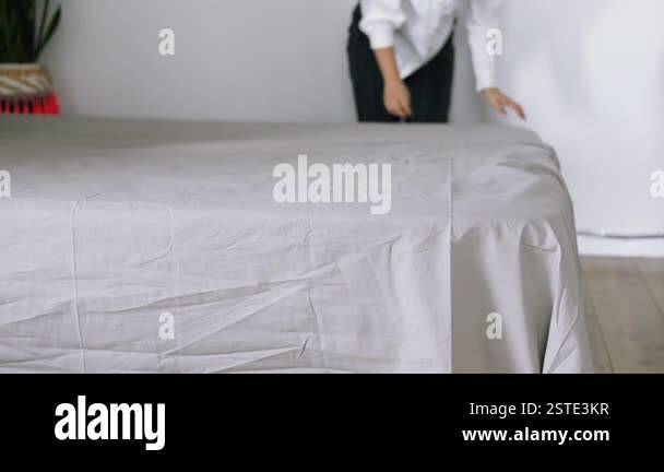 Woman makes the bed, fluffing soft pillows on bed in the bedroom. Young ...