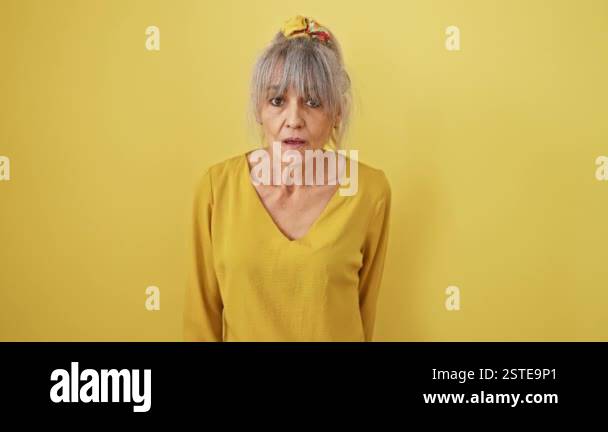 Angry middle-aged woman with grey ponytail furiously pointing at camera ...