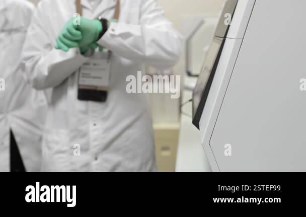 A scientist in a medical gown and protective gloves stands near a ...