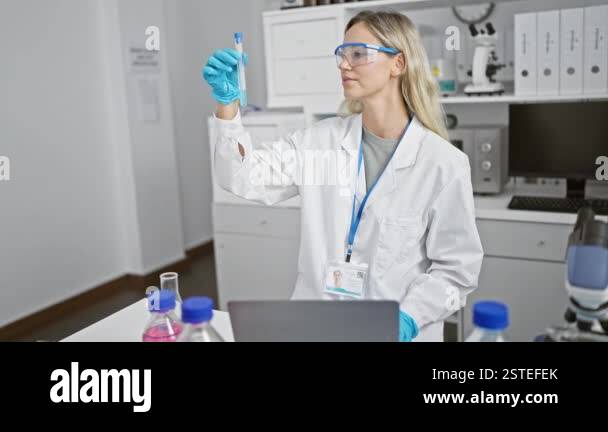 A young caucasian woman in lab attire analyzes a test tube in a modern ...