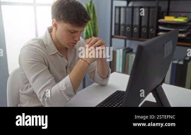 Young man working intently at a computer in a modern office, surrounded ...