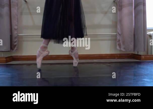 Ballet dancer as she practices exercises on dark stage or studio ...