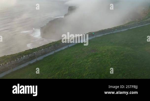 Aerial. Tourists walk along the misty road of the Cliffs of Moher. Mum ...