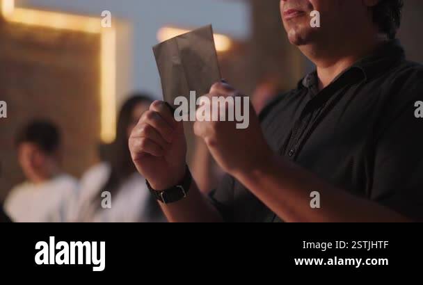 Man and woman holding offering envelopes during worship service, illuminated cross on church ...