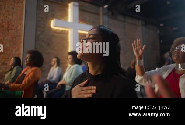 Women singing in prayer during church service, one raising hand in ...