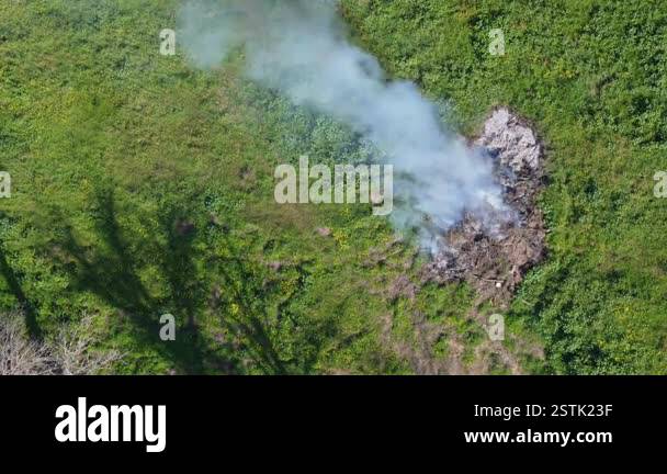 A controlled fire is actively burning in a grassy area, producing smoke ...