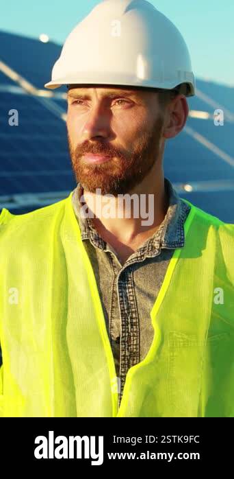 A construction worker in a hard hat stands in front of solar panels ...
