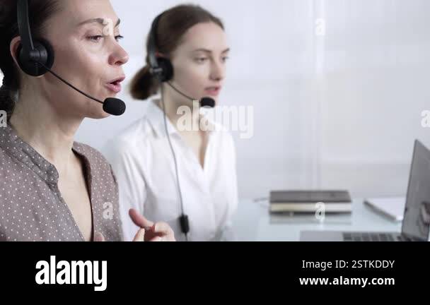 Focused female call center operator in brawn dotted blouse is assisting clients online ...