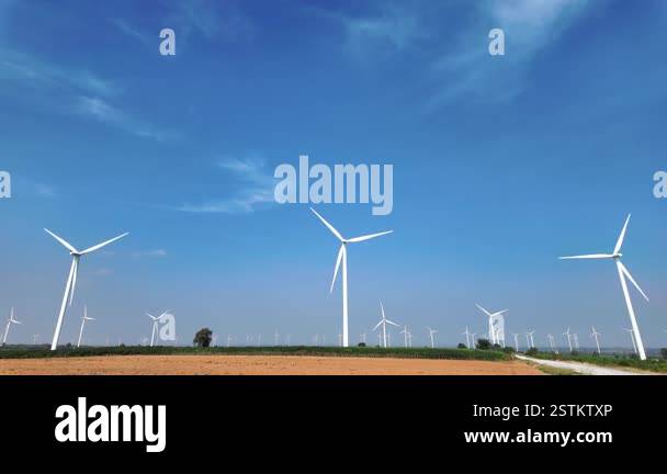 Vast wind farm with multiple turbines spinning under a clear blue sky ...