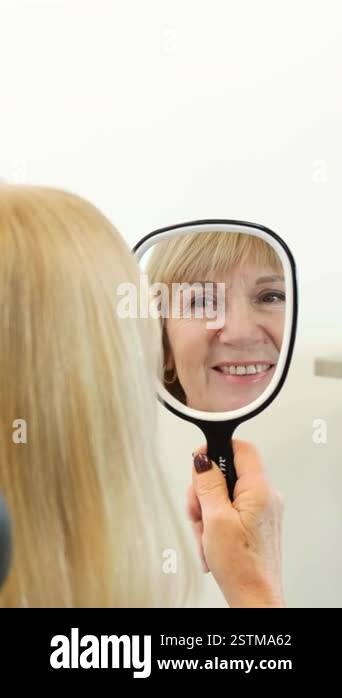 A woman gazes and smiles at her reflection in a mirror, showcasing her ...