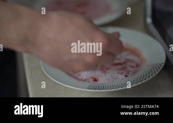 A mans hand mixes strawberry puree with milk in a plate with a spoon ...