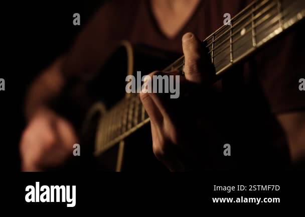 A detailed view of hands plucking strings on an acoustic guitar in dim ...