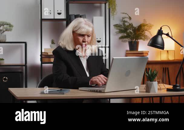 Angry furious elderly businesswoman freelancer using laptop working at ...