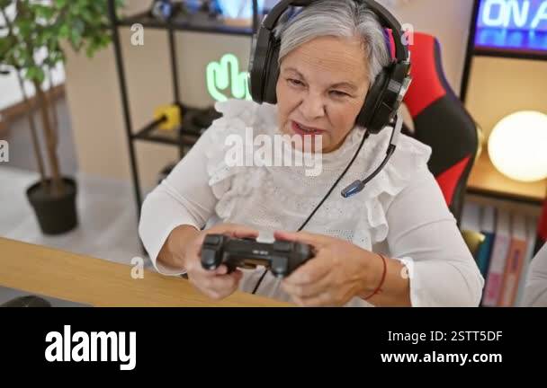 Senior woman happily gaming in a modern room with headset and ...