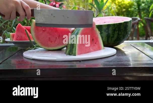 Close-up of hand slicing juicy red watermelon with vibrant green rind ...