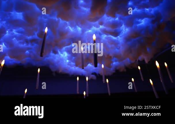 Magic flying candles lamps hanging under ceiling decorated with blue led clouds. Glowing ...