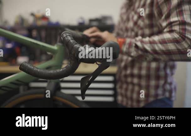 Bicycle mechanic works at his repair shop, wrapping handlebar tape on a gravel bike. The ...