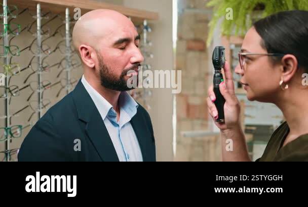 An optometrist performs an eye exam on a patient using a handheld ...