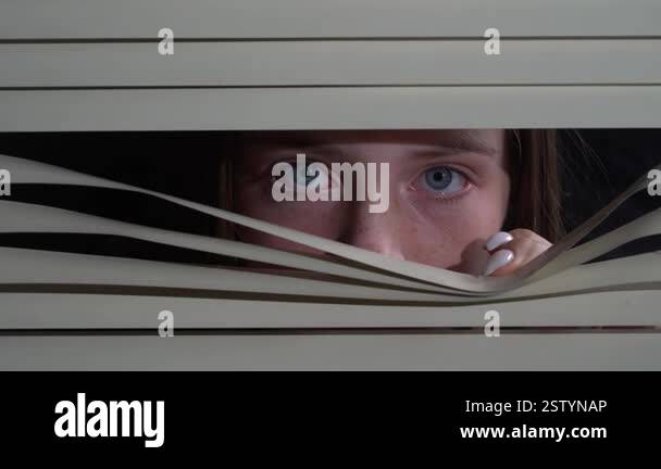 Close up front portrait from indoors of young girl pushing blinds at ...