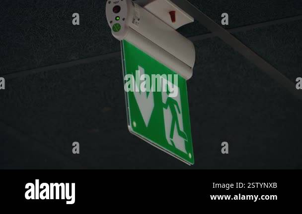 Green exit sign hanging from the ceiling, illuminated and glowing in ...