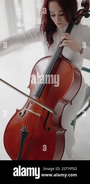 A beautiful woman sitting and playing the cello in a studio on a white ...