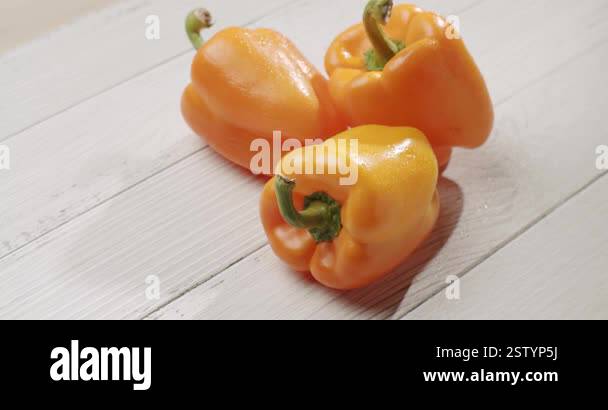 Three fresh yellow bell peppers on a white wooden surface, captured in ...