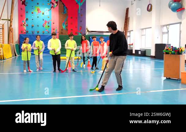 Gym teacher showing floor hockey dribbling technique to elementary ...