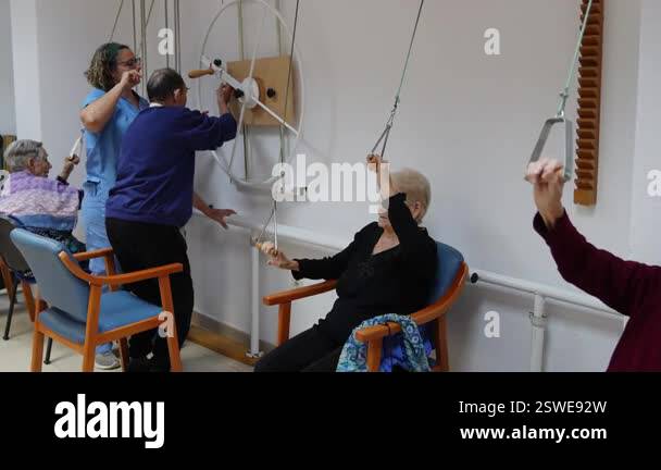 Assisted by nurses, an elderly woman engages in upper body exercises ...