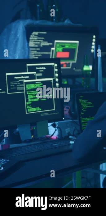 In a dim room, a hoodieclad figure works at a computer, the monitors ...